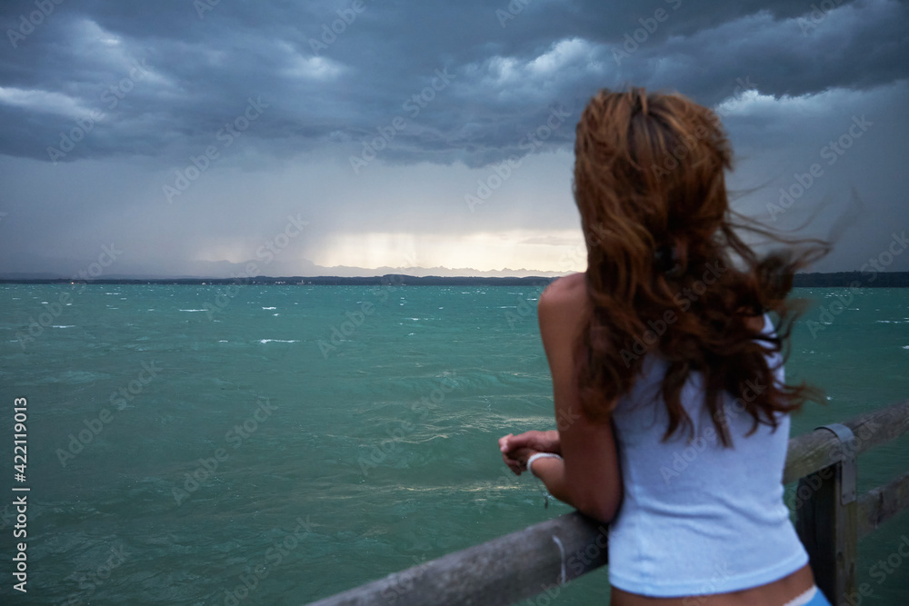 Young woman stands on a parapet on a pier and looks over the water. In ...