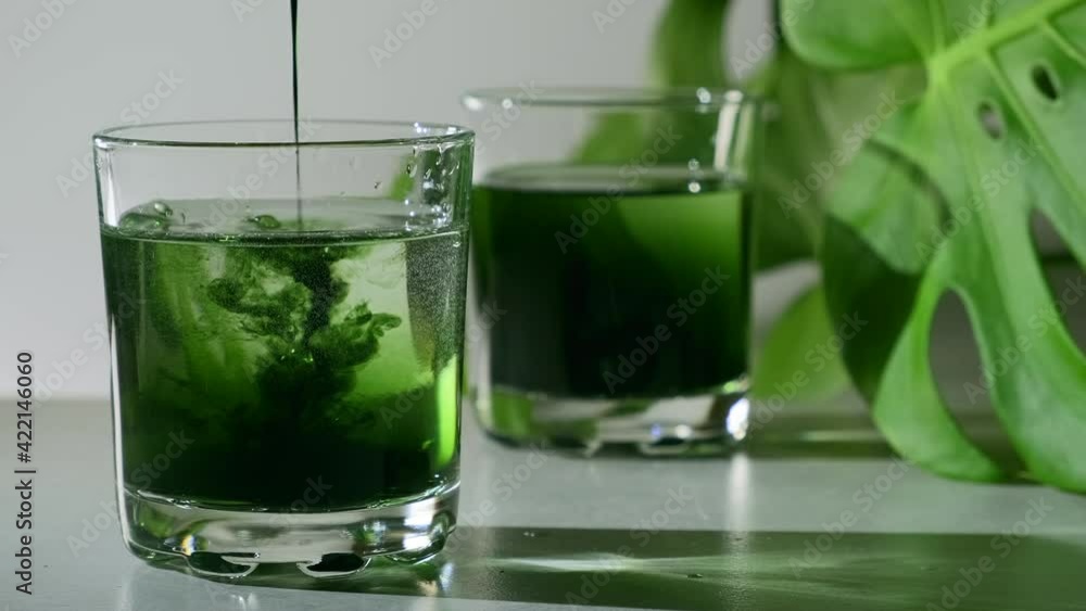 Chlorophyll extract is poured in pure water in glass against a white ...