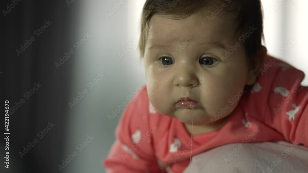 Little girl in mom's arms. The baby looks into the camera and saliva ...
