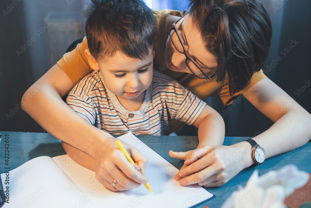 Caucasian helpful mother is teaching her son to write holding his hand ...