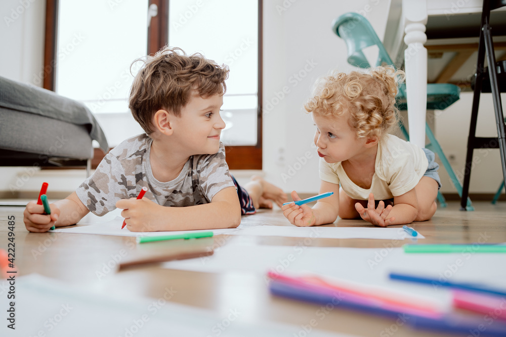 Little boy and girl draw together in white room with window. Kids doing ...