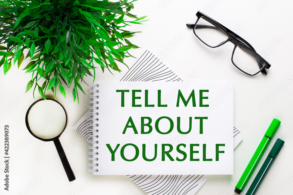 On a white background lies a notebook with words TELL ME ABOUT YOURSELF ...