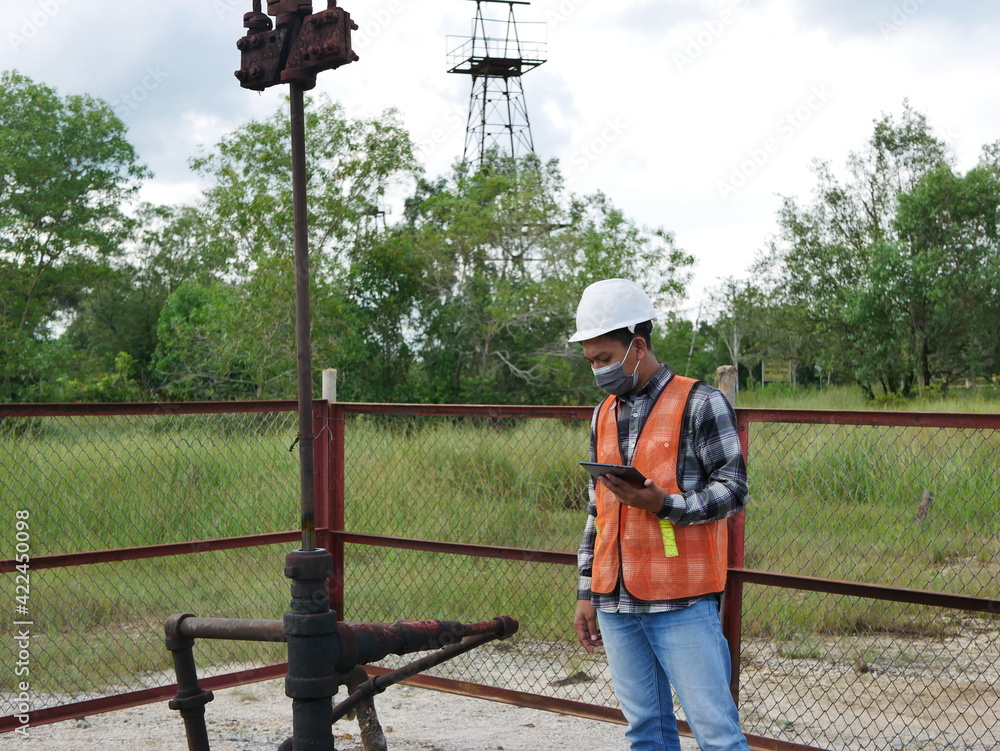 An Indonesian engineer wearing hard hat helmet checking oil derrick ...