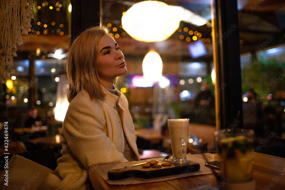 Beautiful woman sit in night cafe and eat fast cafe and dink coffee in ...