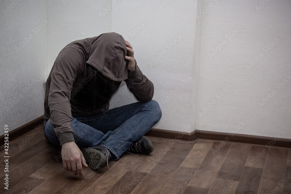 desperate young drug addict wearing hood and sitting alone in corner ...