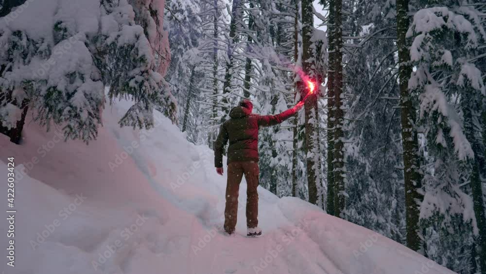 man walking in dense snowy frosty forest waving signal flare, adventure ...
