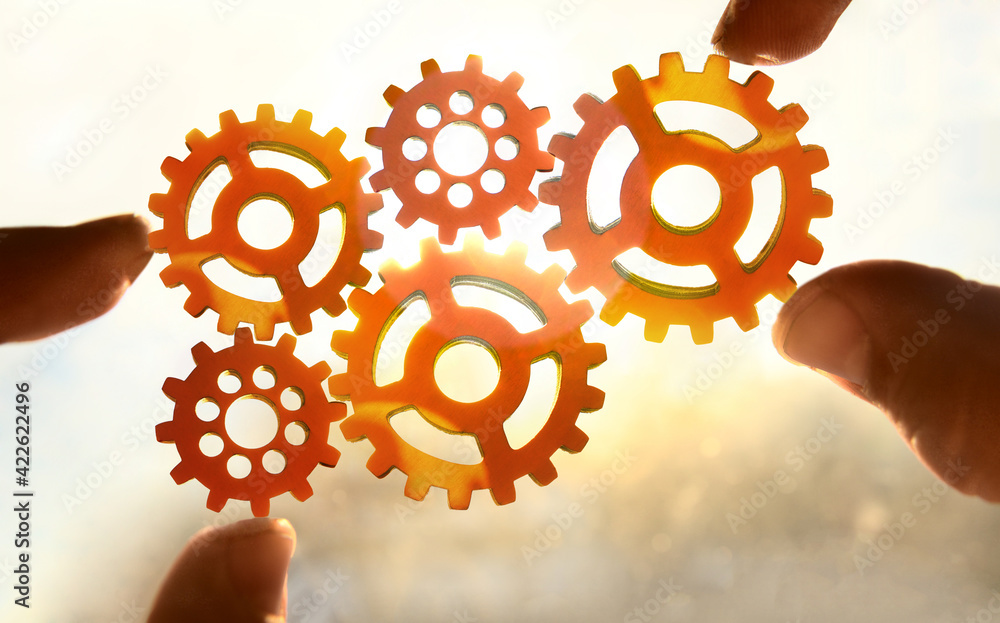 Male hand holding five 5 wooden cog wheel, gear wheel on golden sky ...