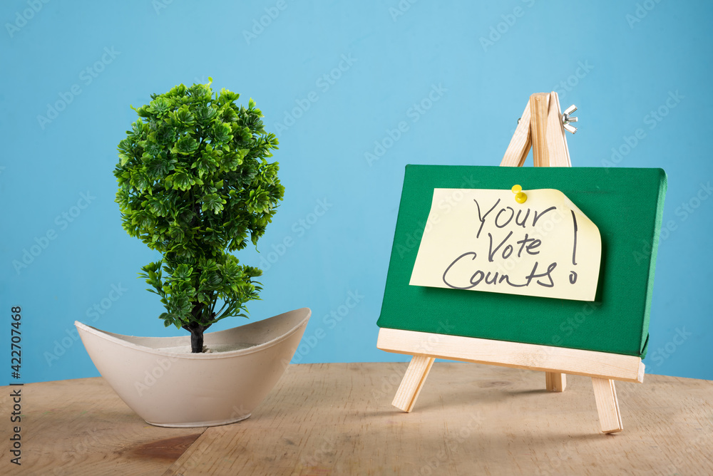 Your vote counts written on a sticky note on a mini green notice board ...