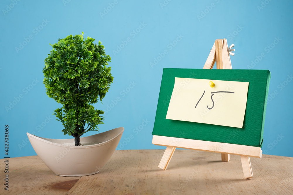 15 written on a sticky note on a mini green notice board with a plant ...