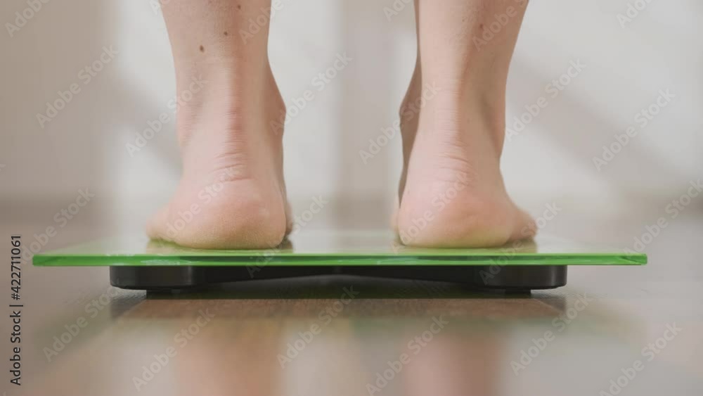 Female feet step on floor scales close up back view. Woman measuring ...