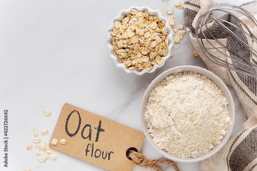 Oat flour and oat flakes on white marble background with a brown tag ...