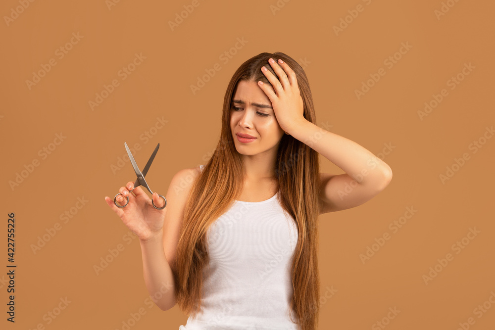 Unhappy young lady looking at scissors and grabbing her head in ...