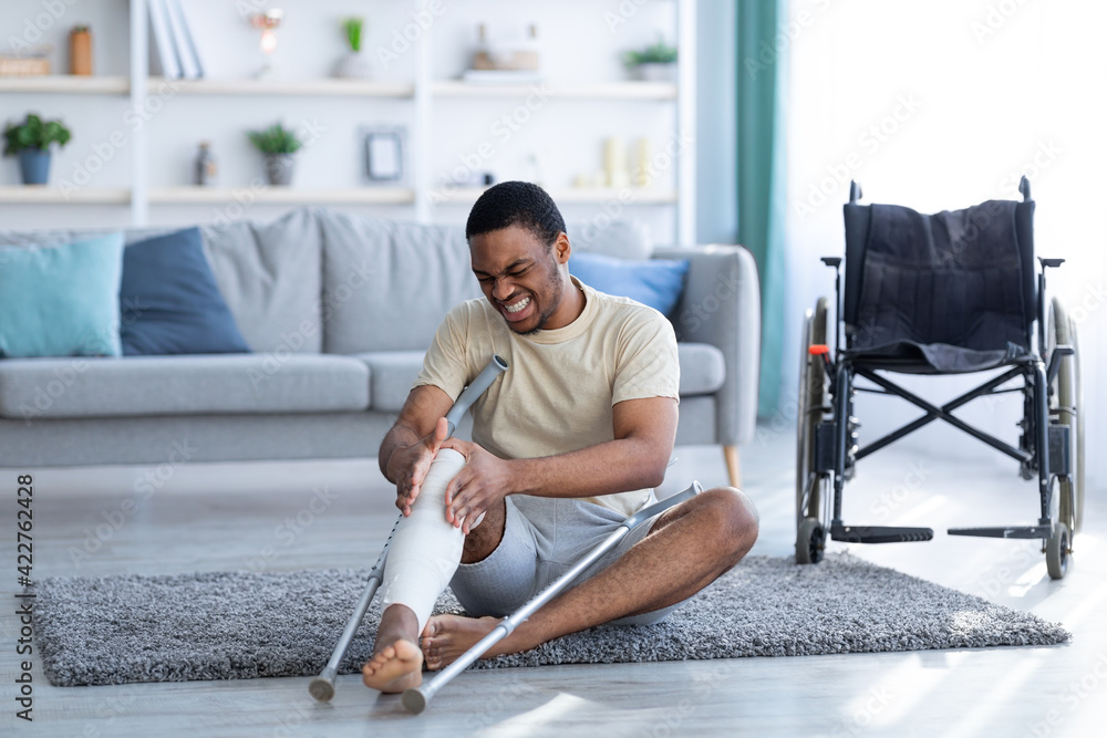 Young black man suffering from pain in plastered broken leg, sitting on ...