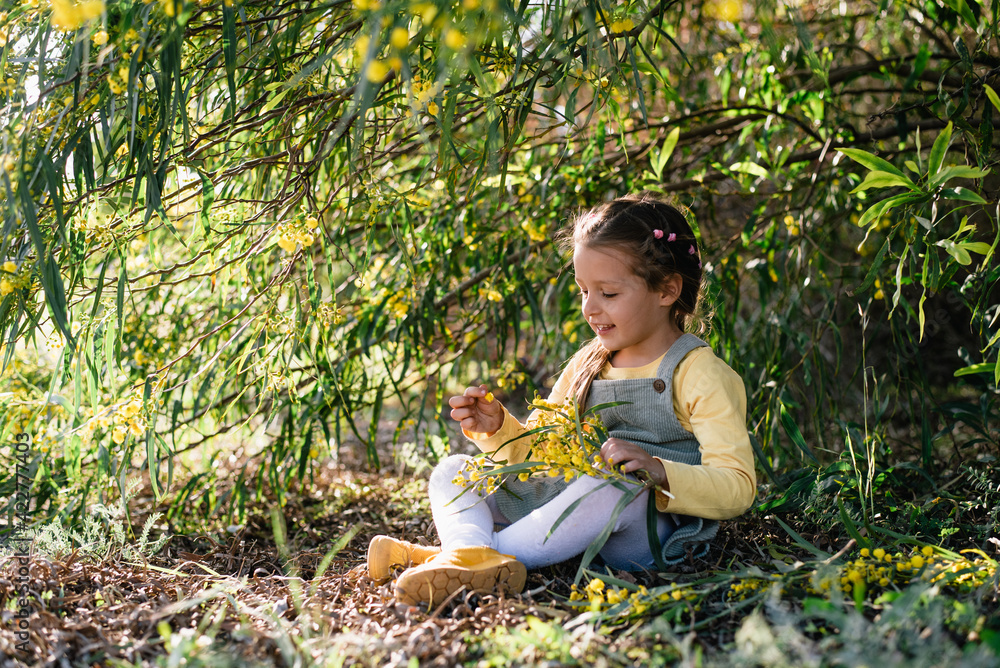 Little girl in yellow t-shirt and sneakers sitting near flowering ...