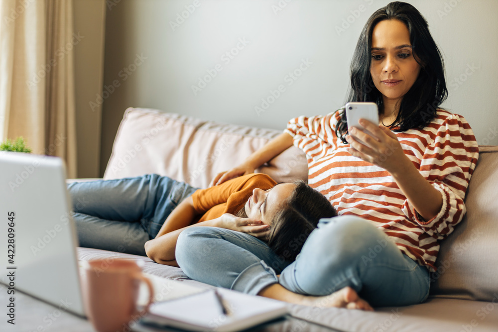 Single Mother Working At Home With Her Preteen Daughter Lying On Her