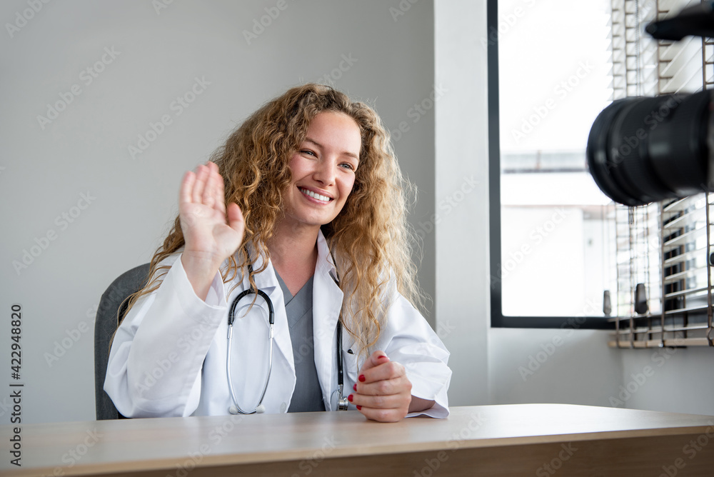 Smiling cheerful Caucasian woman doctor waving hand to camera while ...