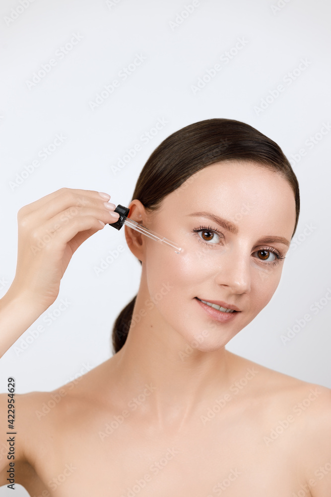 Female applying anti wrinkle serum on face, looks in camera smiling ...