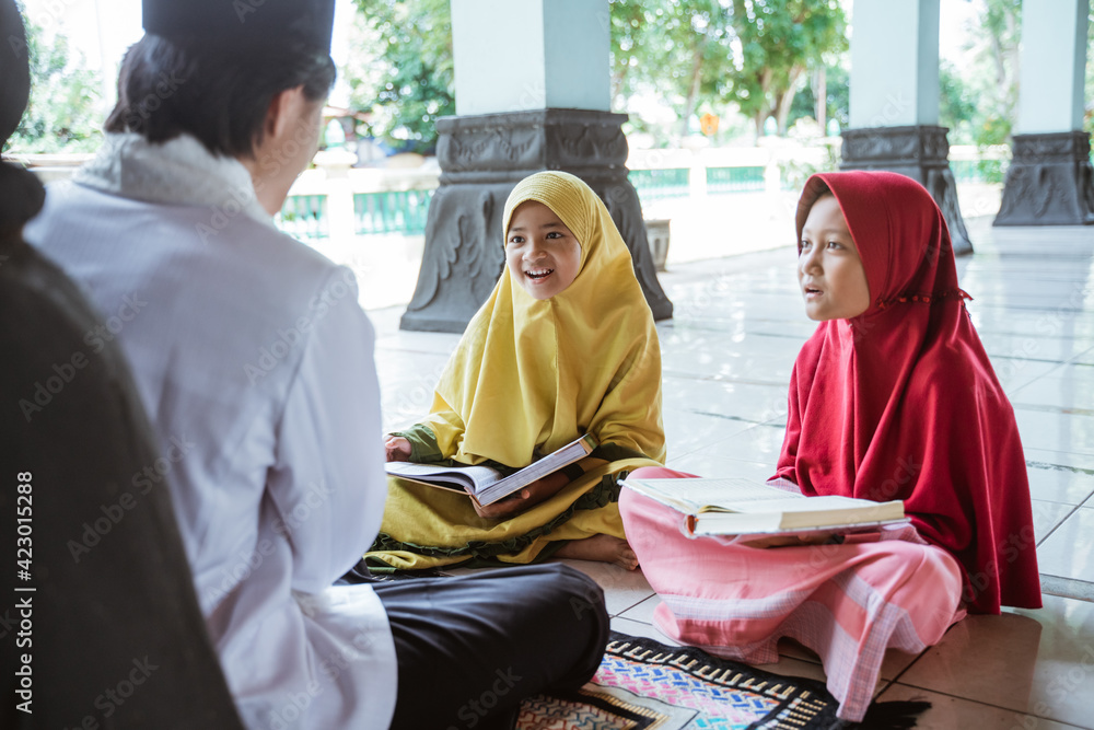 two kids learning to read quran with muslim teacher or ustad in mosque ...