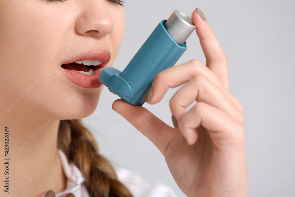 Young woman with inhaler having asthma attack on grey background ...