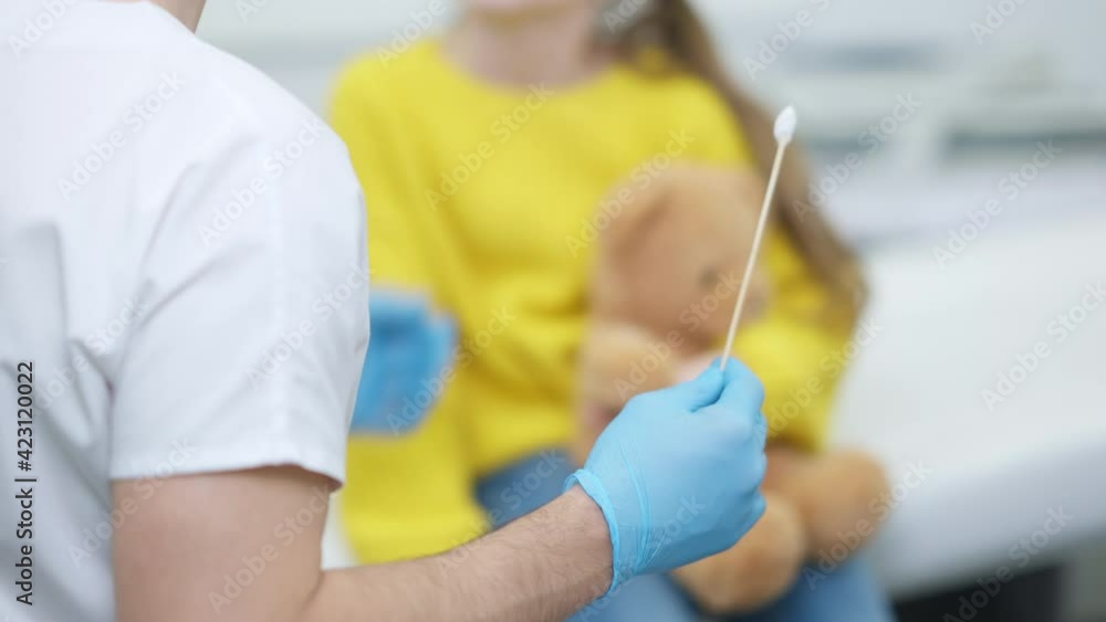 Close-up of cotton swab in doctor hand with blurred little girl at ...