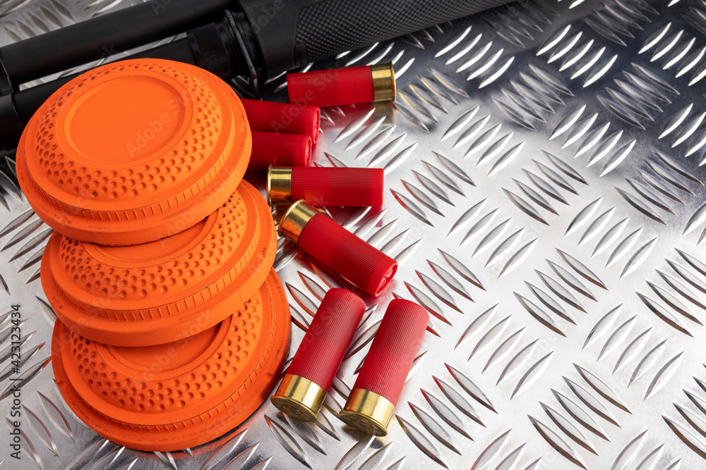 Clay disc flying targets and shotgun shells on metal texture background ...