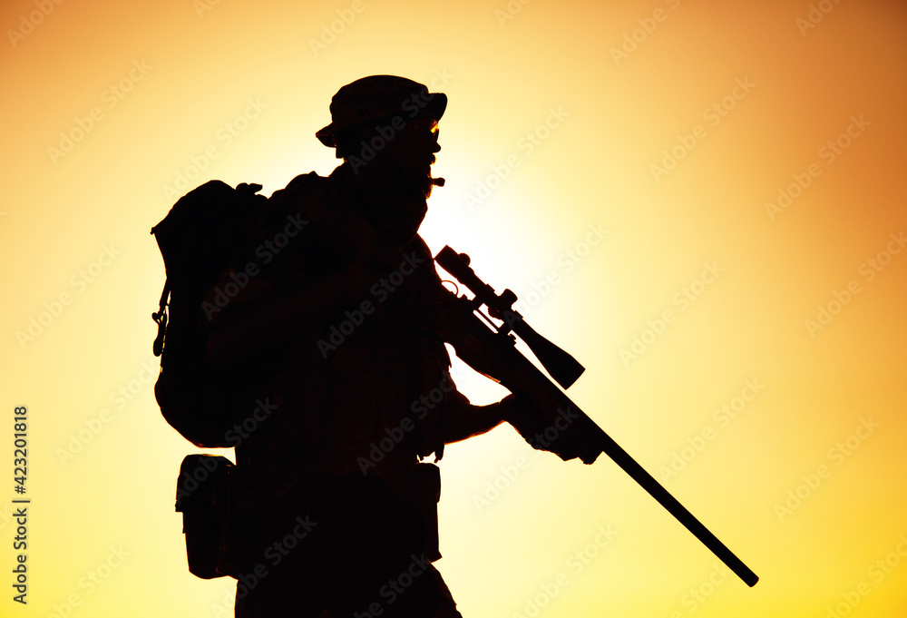 Silhouette of army elite forces sniper, commando shooter in boonie hat, carrying backpack ...