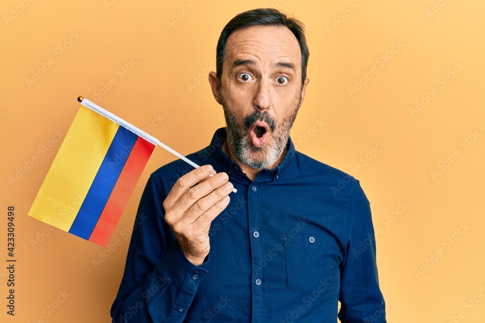 Middle age hispanic man holding colombia flag scared and amazed with ...