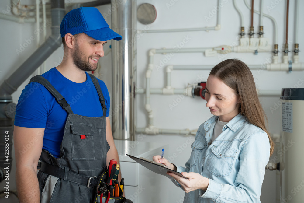 A female client signs a bill from a male plumber standing in the boiler ...
