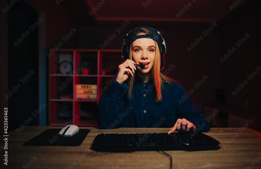 Cute girl streamer in a headset and cap plays video games at home and ...