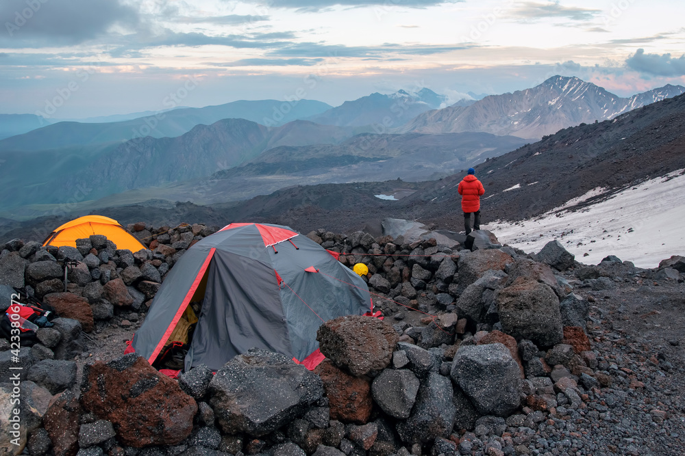 Alpine camp. Two tents above surrounded by stone wall and climber in ...