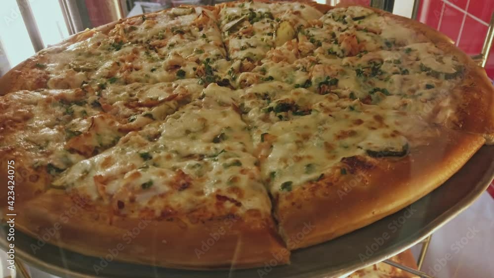 Closeup of fresh large crust pizzas in store cafe on rotating display ...