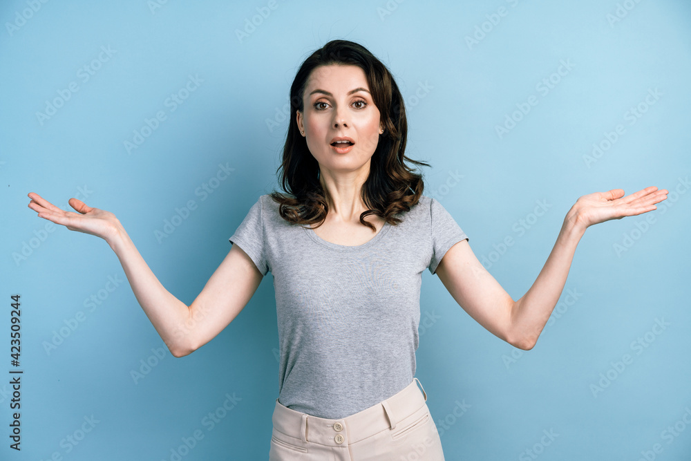 Confused girl with open arms doubts on a blue background. Isolated on ...