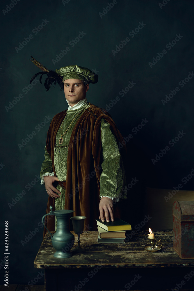 Renaissance man stands behind a table with books on it, a tin pitcher ...