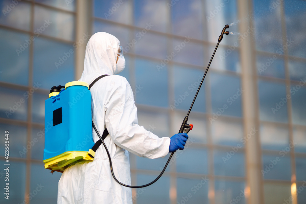 Man in Hazmat suit, protective gloves and goggles use sprayer equipment ...