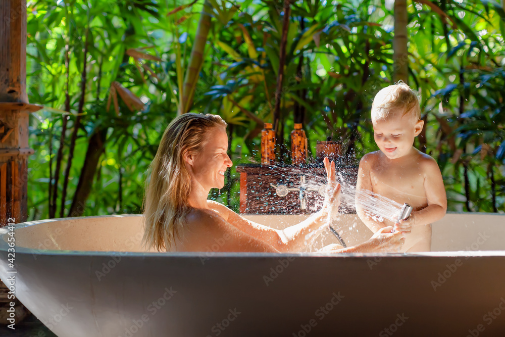 Happy baby son with mother have fun in bath. Playful woman spraying ...