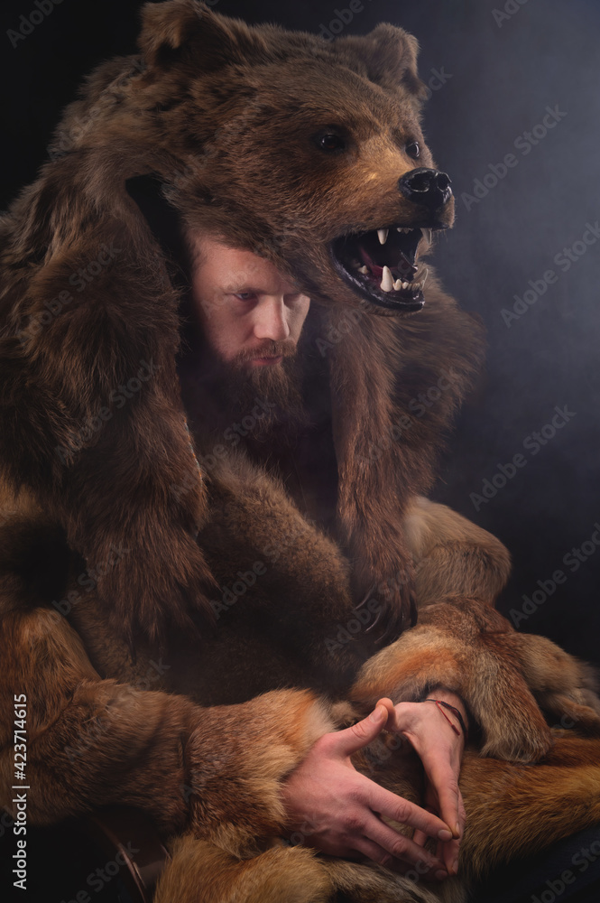 A male shaman werewolf in the skin of a bear sits in a dark room and ...