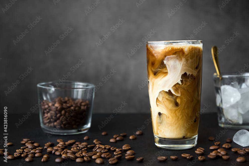 Iced coffee in tall glass with cream, container with ice and spoon ...
