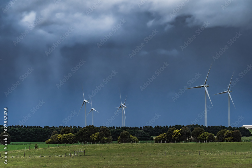 Rain falling from dark stormy skies hovering over tall wind turbines ...