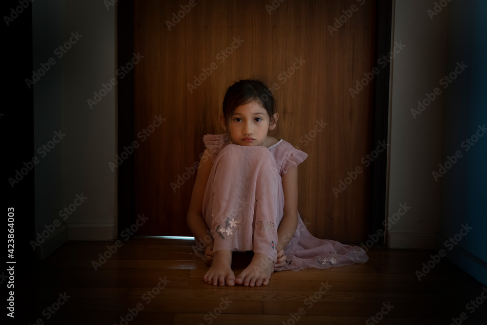 Sadness offended little girl scared. A Child sitting in a dark corridor ...
