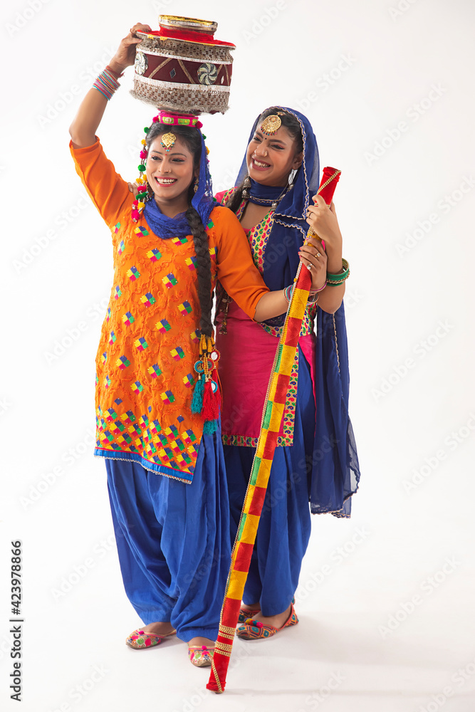 Two Giddha dancers standing together holding decorated matki and stick ...