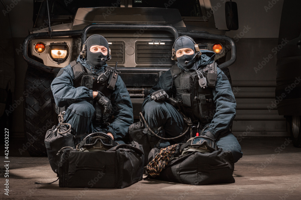 Two uniformed commandos sit in a hangar with a military truck in the ...