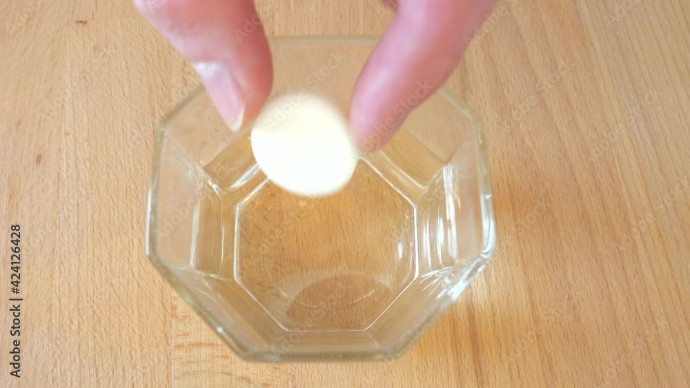 Hand drooping a pill effervescent tablet in a glass of water ...