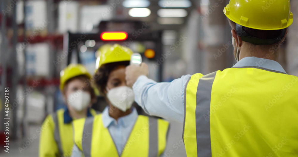 Manager measuring body temperature of warehouse workers with infrared ...
