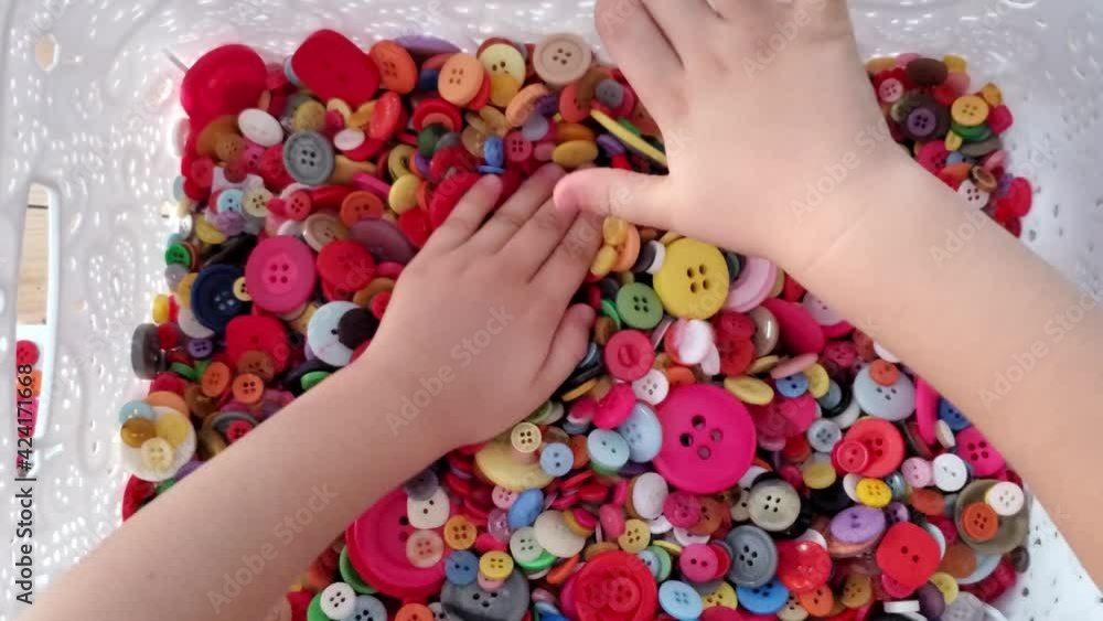 Hands of little girl playing with colorful buttons in box. Sensory game ...