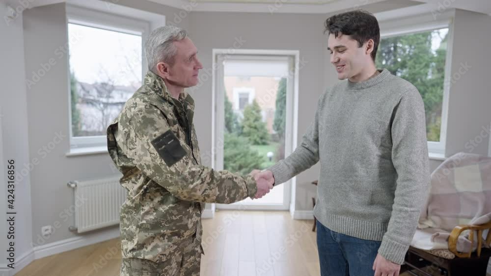 Middle aged military father and adult son talking and shaking hands ...