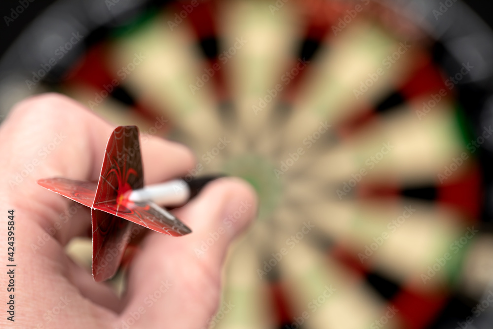 Close-up of man hand holding red dart at middle of dartboard, which is ...