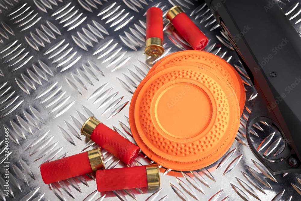 Clay disc flying targets and shotgun shells on metal texture background ...