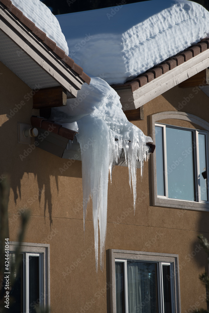 large white frozen icicle in eaves trough suspending from roof top of ...
