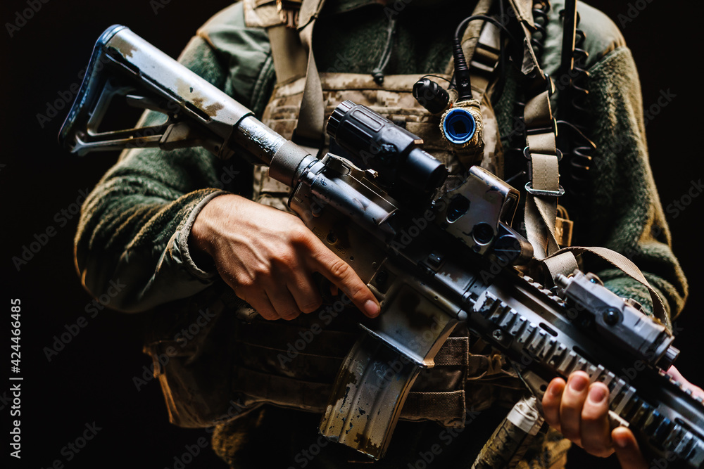 Unrecognizable special forces soldier standing with rifle against black ...
