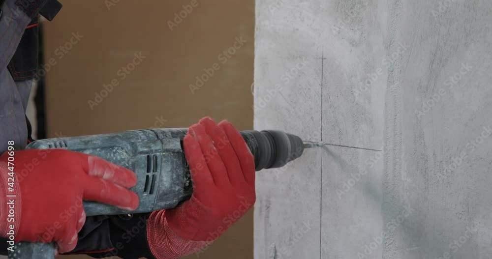 An electrician drills holes in the wall for sockets using a power tool ...